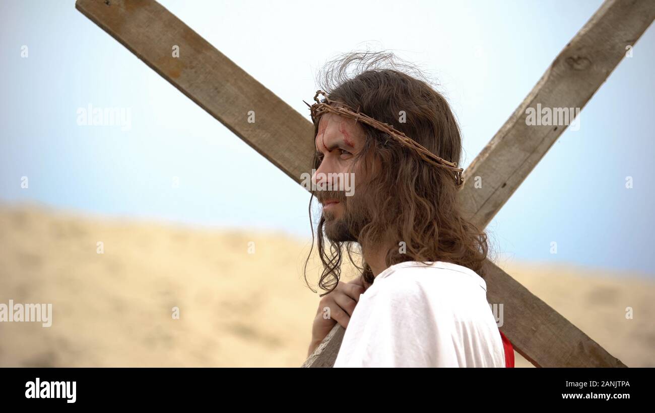 Jesus with bloody forehead and crown of thorns carrying heavy cross ...