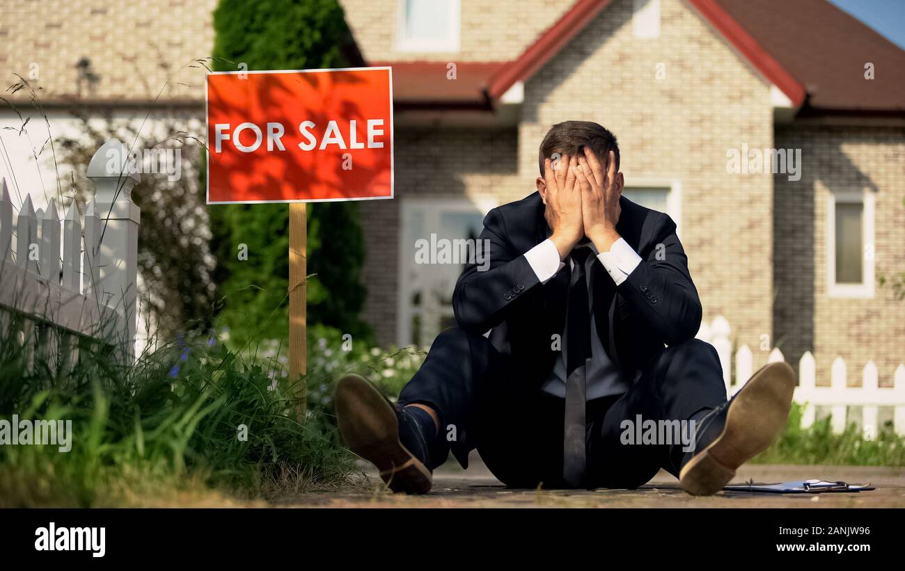 Extremely upset real estate manager sitting by for sale signboard ...