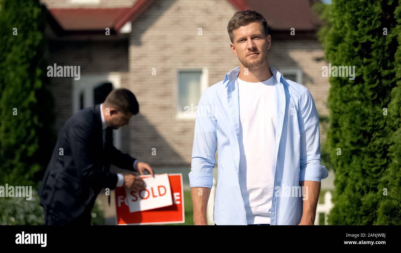 Real estate manager installing sold signboard, new owner looking at ...