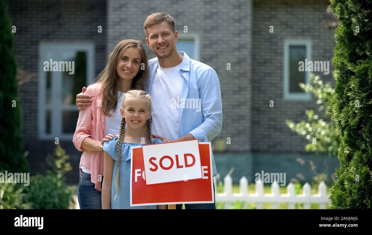Happy family holding sold sign, standing against new bought house ...