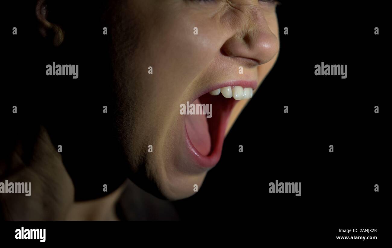 Face of female screaming against dark background, psychological ...