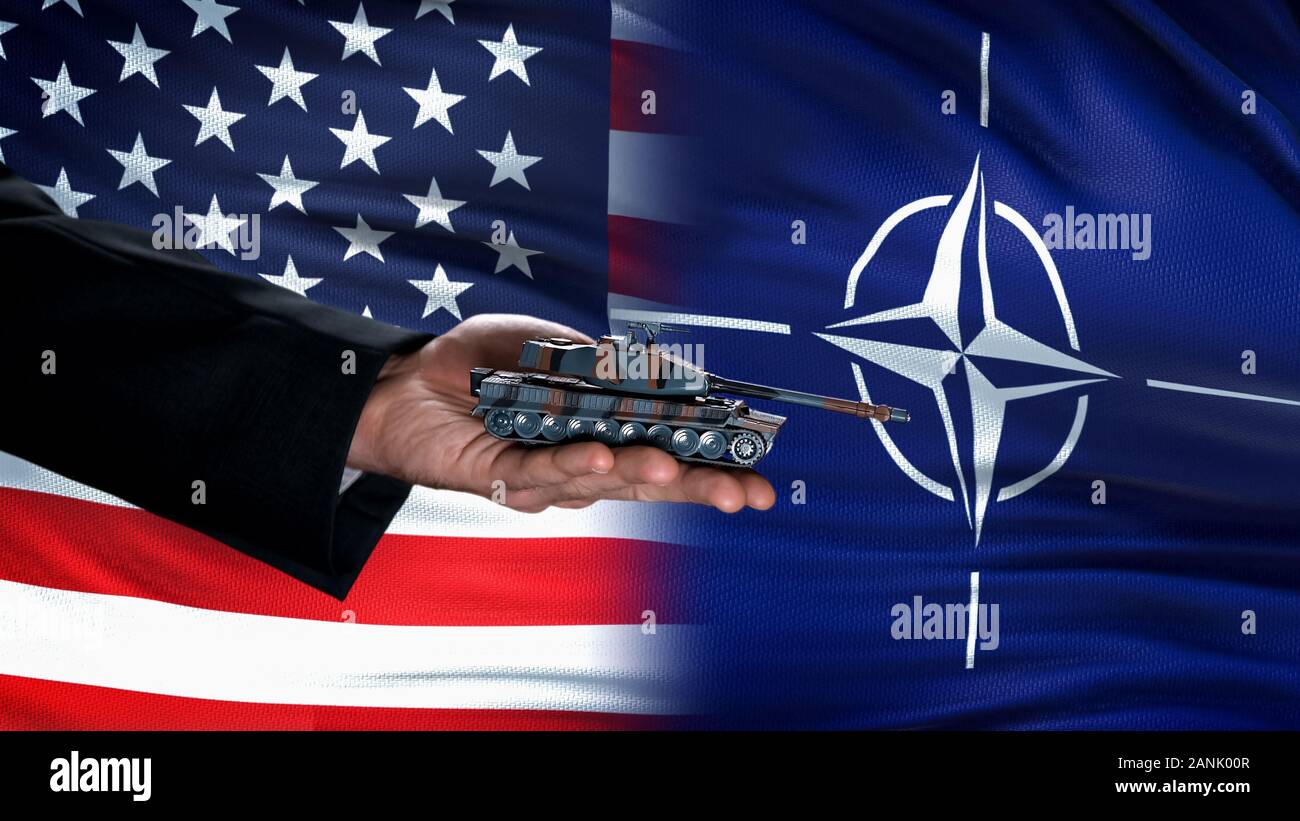 Official hand holding toy tank against USA and NATO flags, weapon trade ...