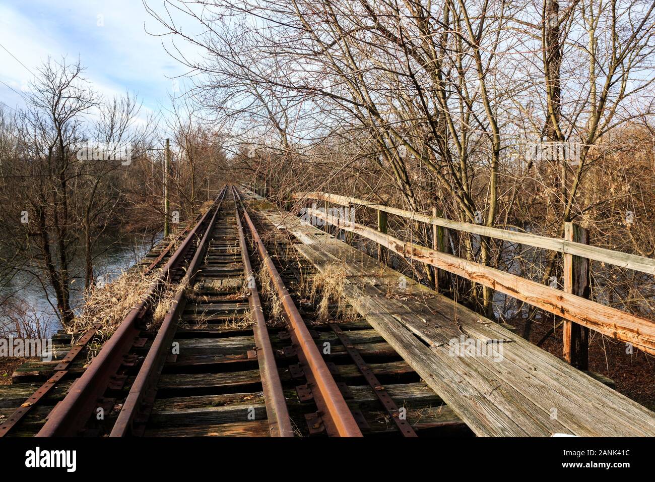 Abandoned railroad bridge and bare trees stretch over a river and into ...