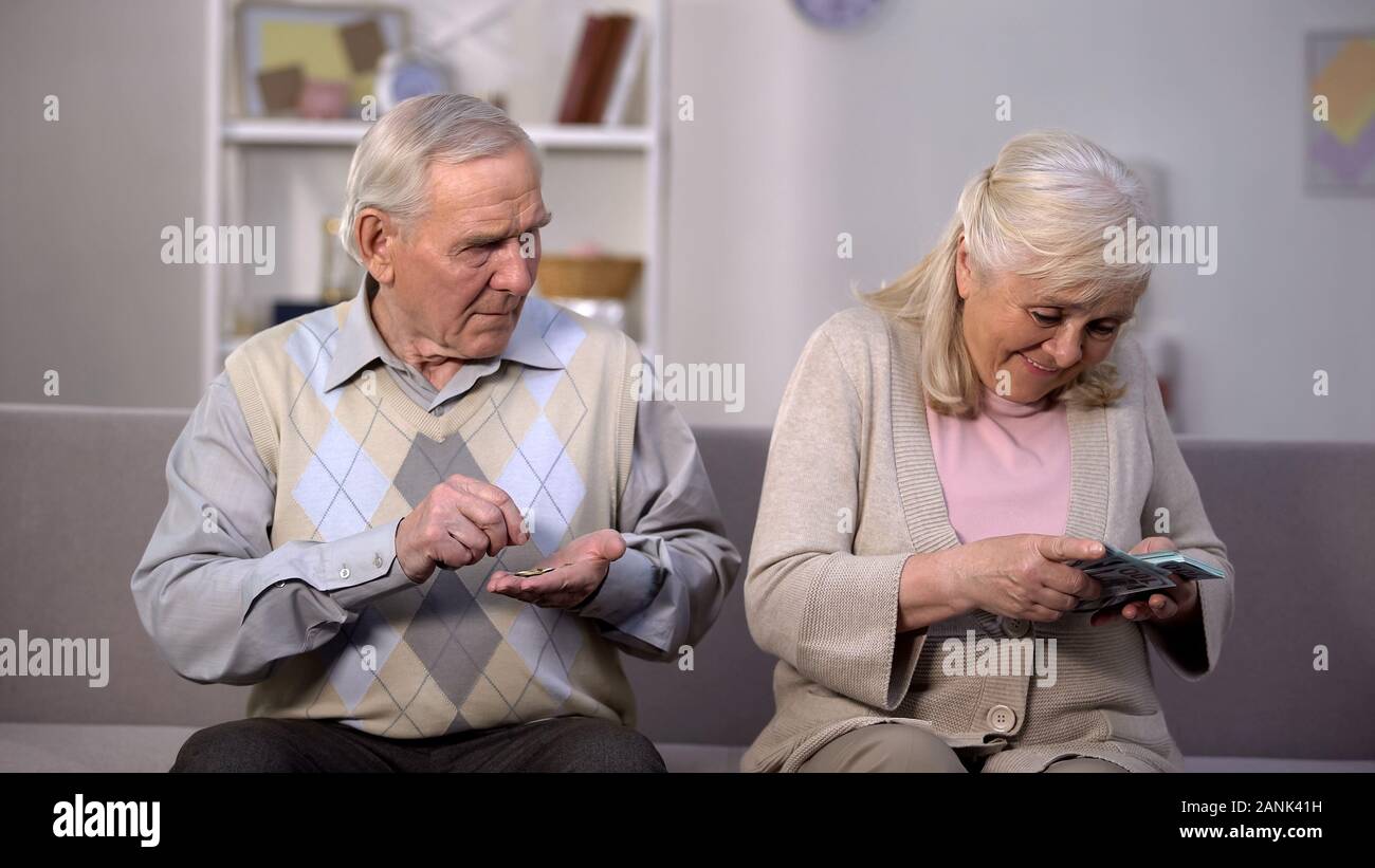 Old man counting coins looking at happy senior woman holding dollars ...