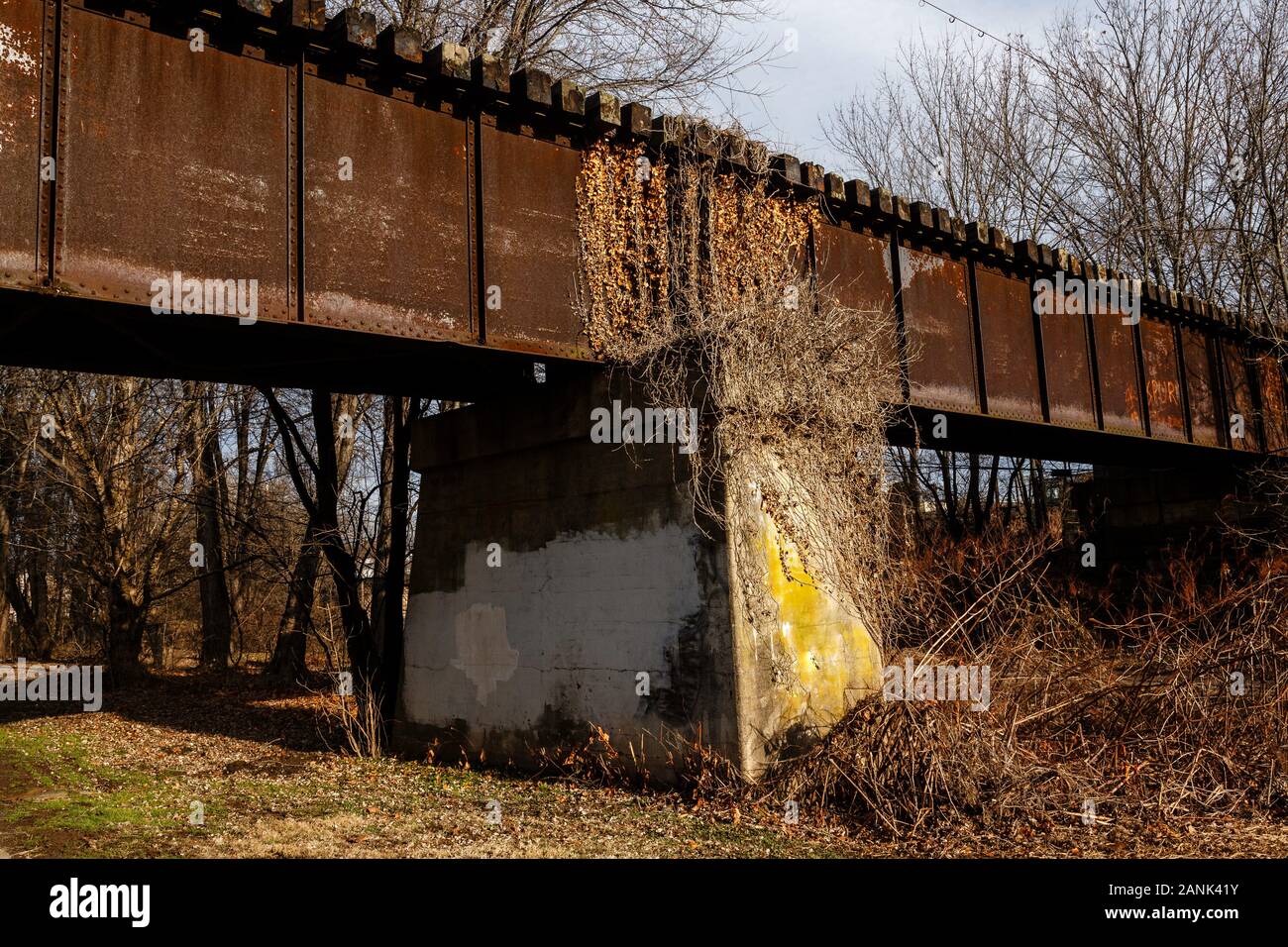 Abandoned, rusted railroad bridge portion rests on a stone abutment ...