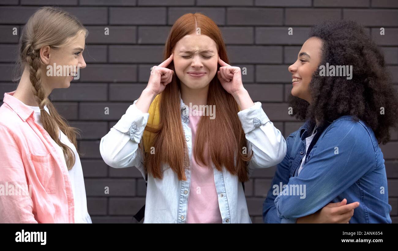 Stressed female teenager covering ears suffering classmates bullying ...
