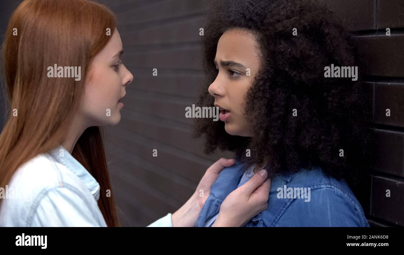 Angry female teenager pushing scared classmate against wall in campus ...