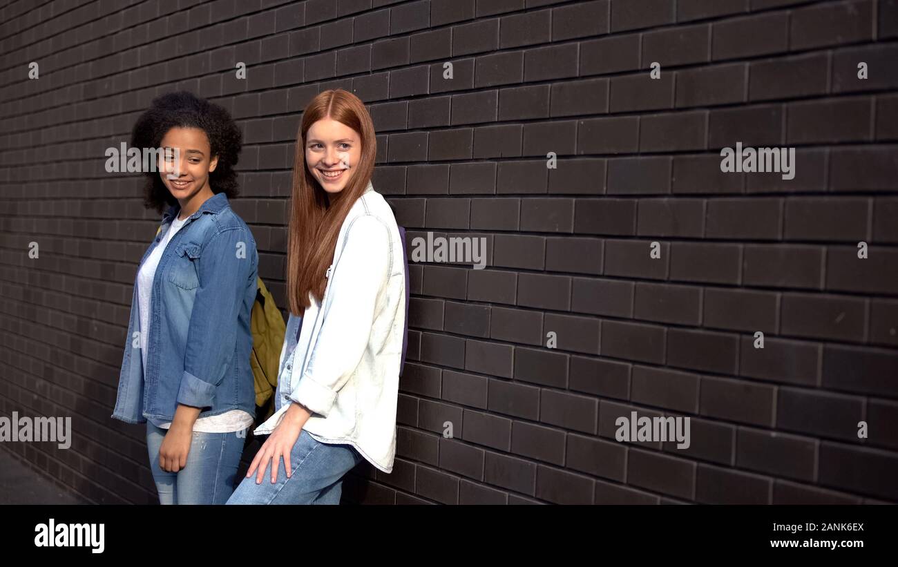 Two smiling university students leaning brick wall, leisure time ...