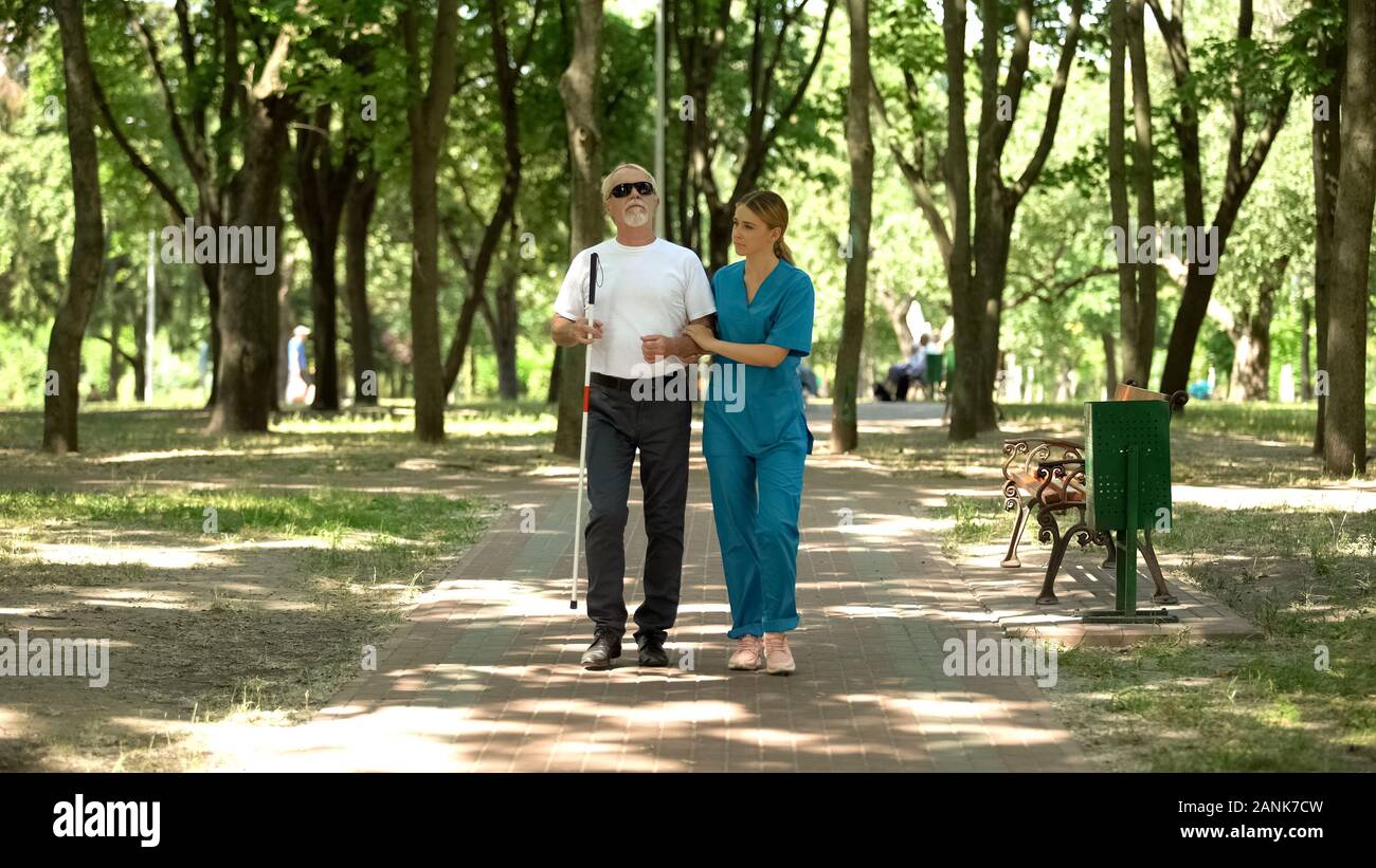 Young nurse holding blind old patient walking in park, vision restore ...