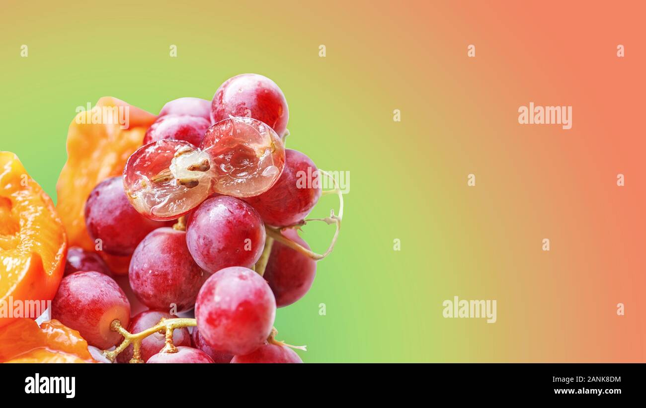 A bunch of ripe pink grapes with a piece of persimmon isolated on a red ...