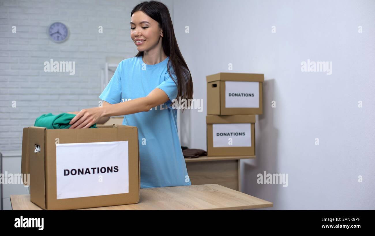 Female volunteer putting clothes in donation box, working in social ...