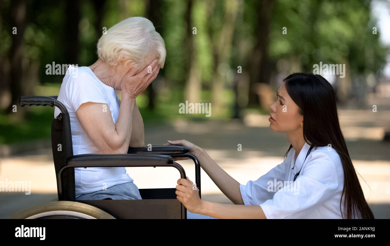 Caring nurse calming crying disabled senior woman in wheelchair, slow ...