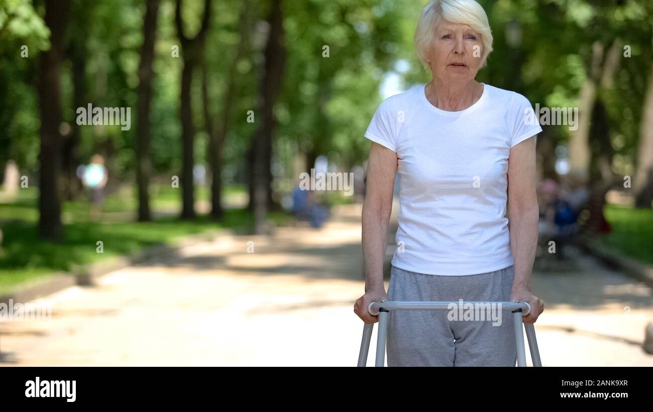 Sad disabled woman with frame walking in park, rehabilitation after ...