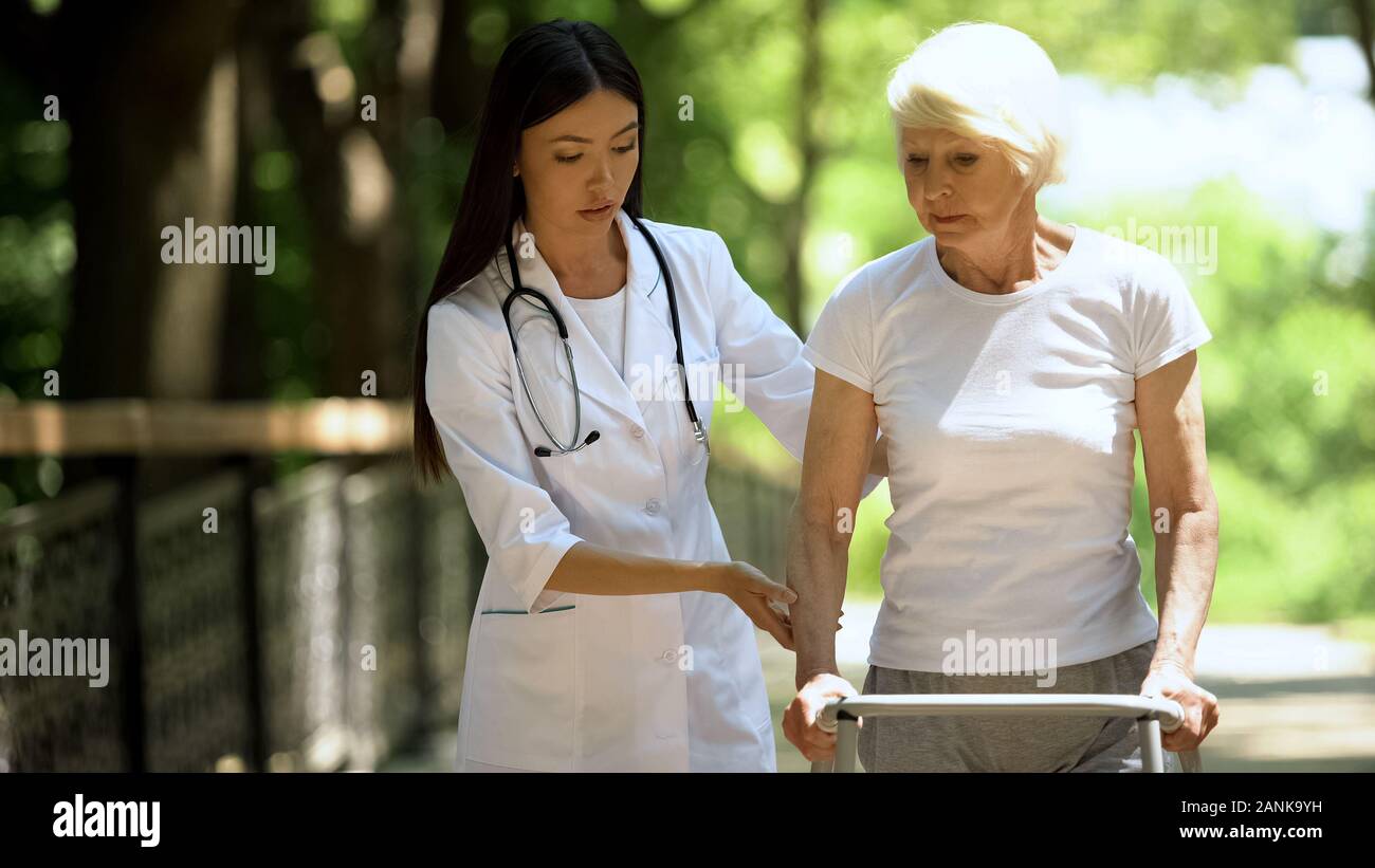 Professional female nurse supporting old woman moving in park with ...