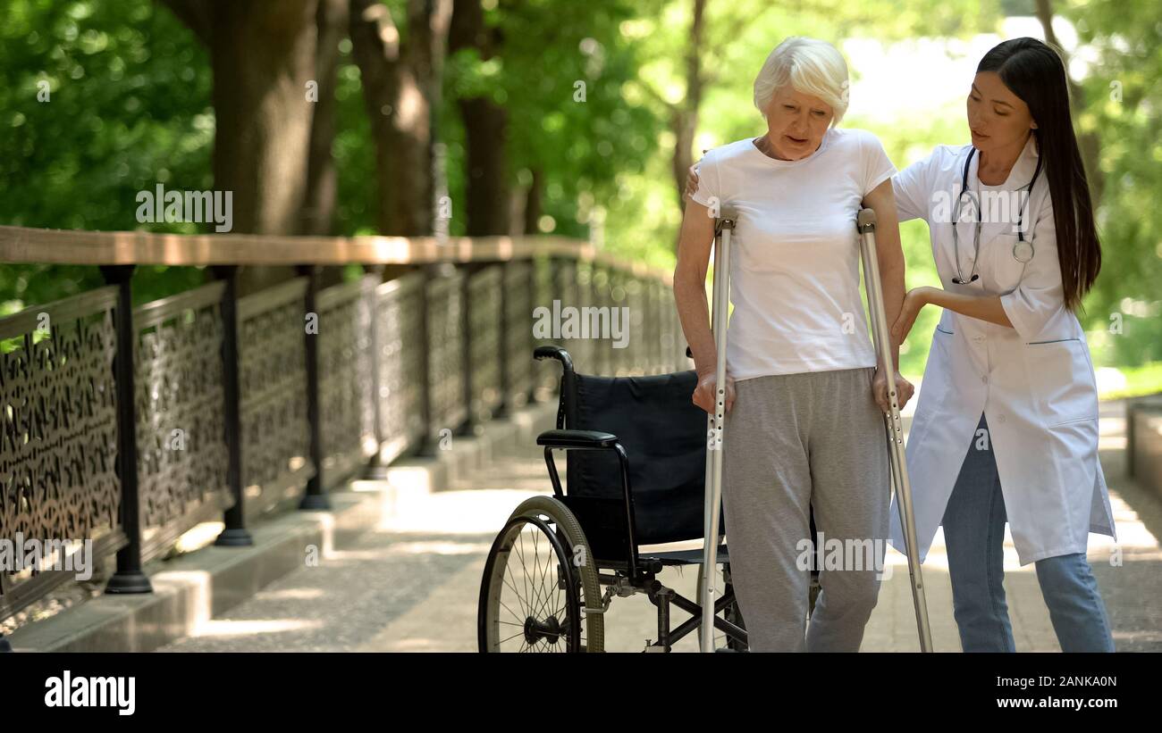 Doctor helping disabled old woman walking with crutches, recovery after ...
