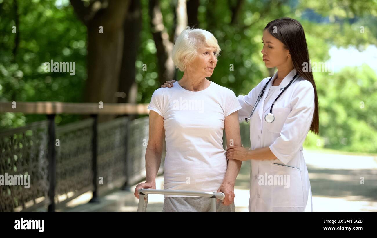 Upset senior woman with walking frame and female therapist looking at ...