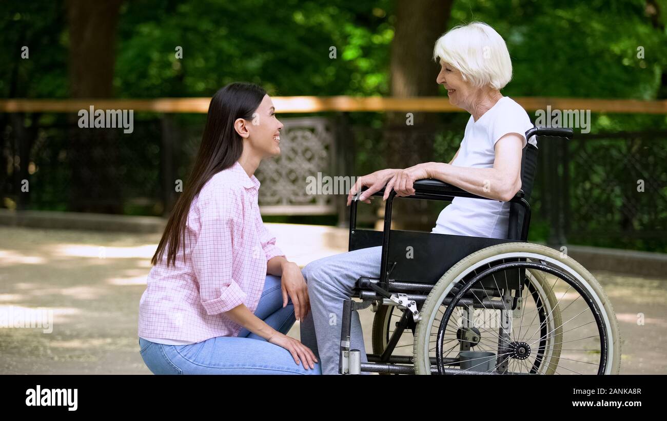 Smiling volunteer talking with old woman in wheelchair, disabled people ...