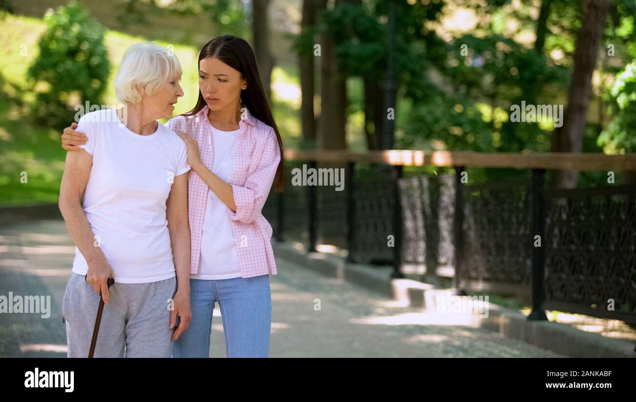 Young woman supporting sick aged lady walking stick, illness depression ...