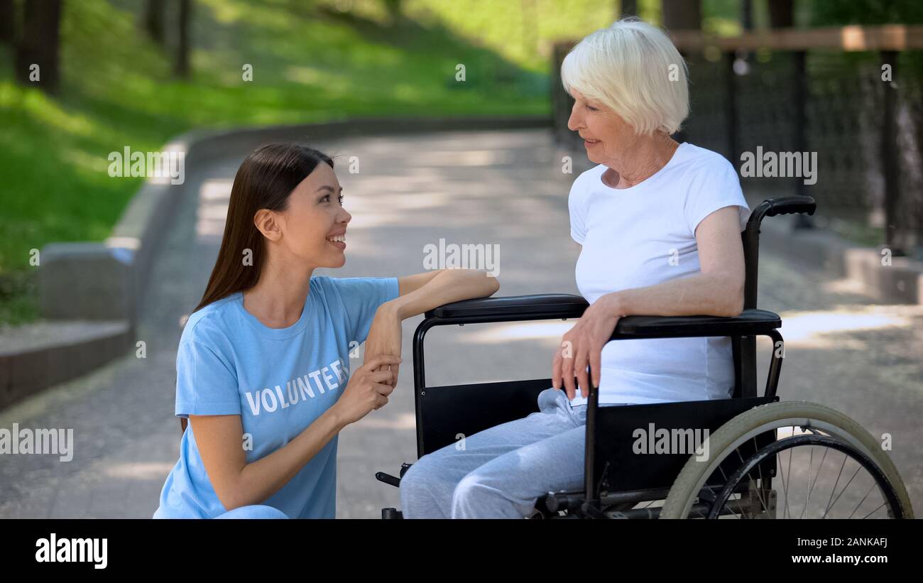Disabled senior lady in wheelchair smiling to volunteer, communication ...