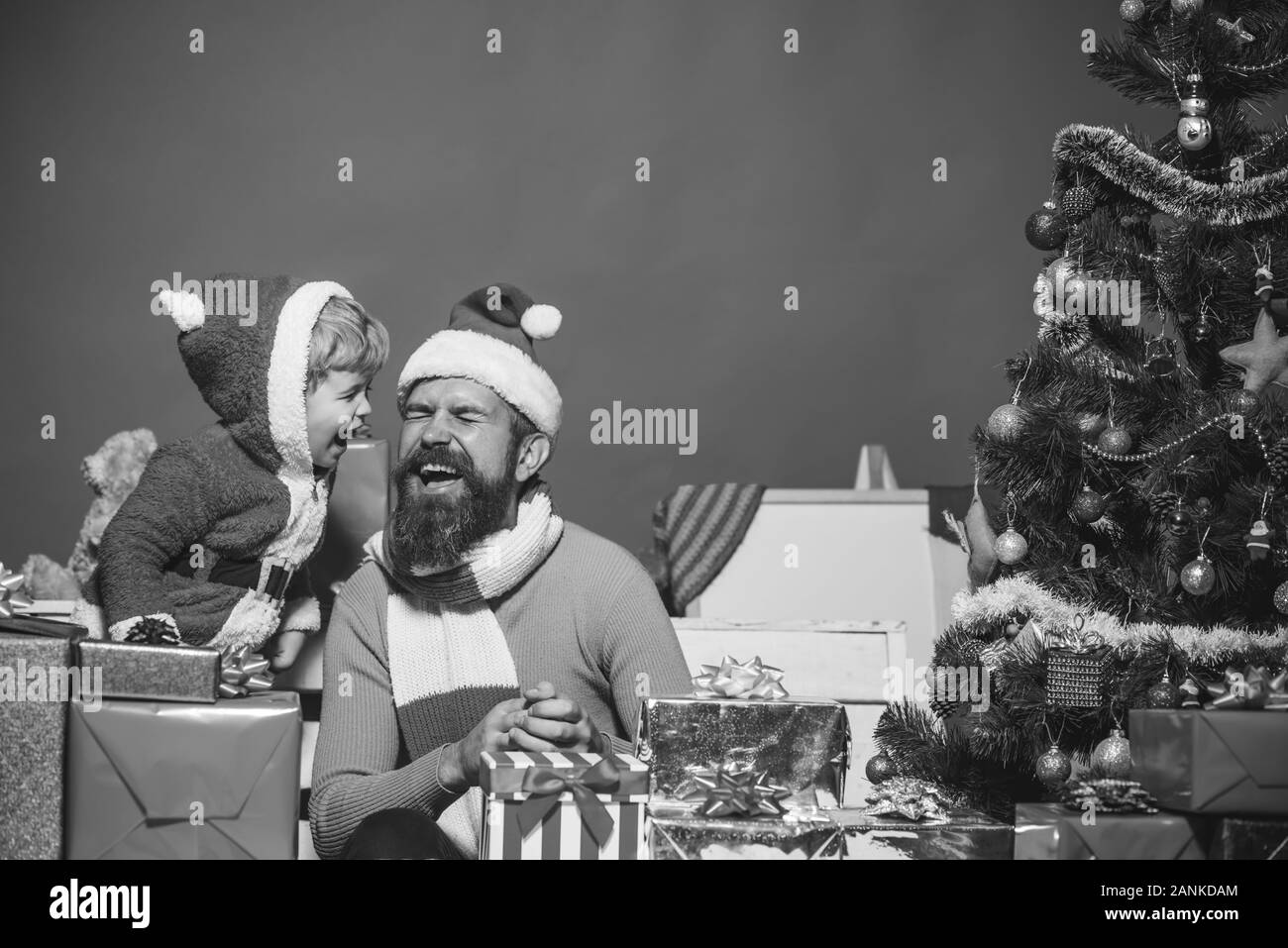 Santa and little assistant among gift boxes by Christmas tree ...