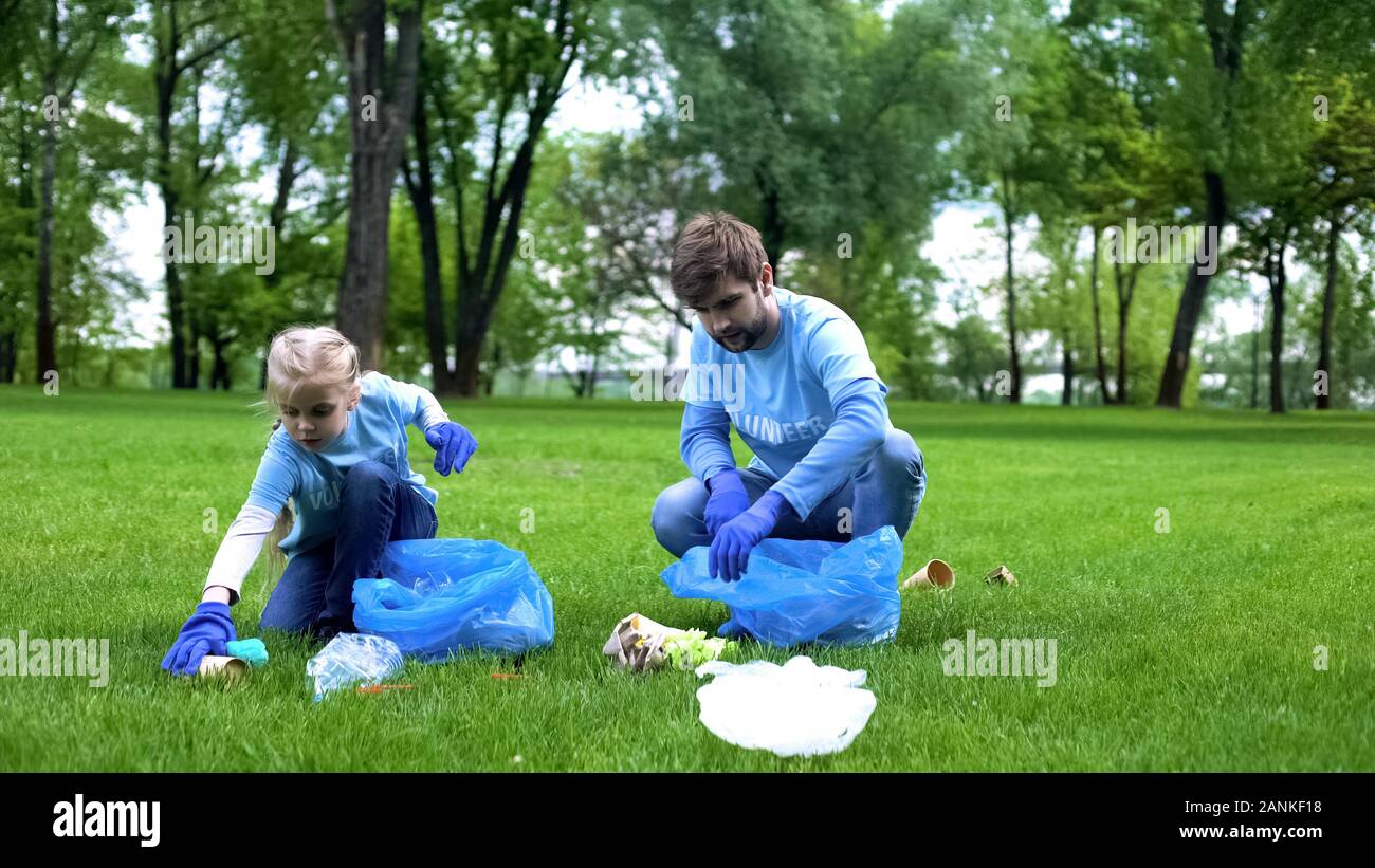 Father and daughter picking up litter in park, participating volunteer ...