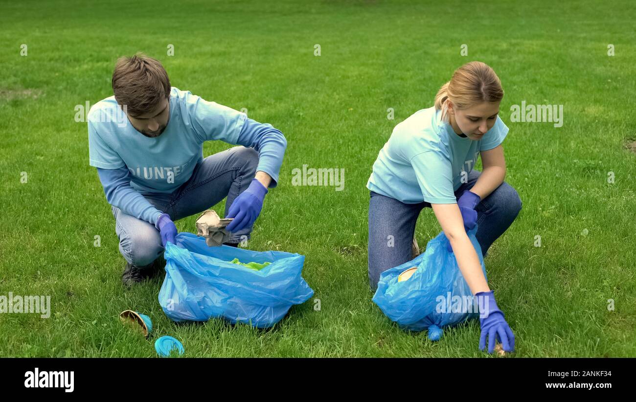 Male and female volunteers picking up litter in park smiling each other ...
