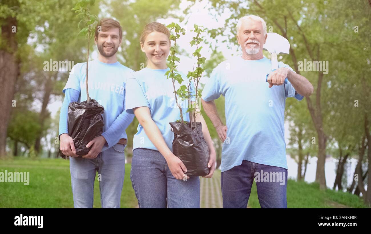 Smiling eco activists holding tree saplings and shovel in hands ...