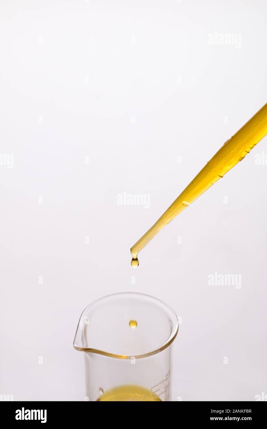 dropping sesame oil from a plastic pipette into a glass beaker, a ...