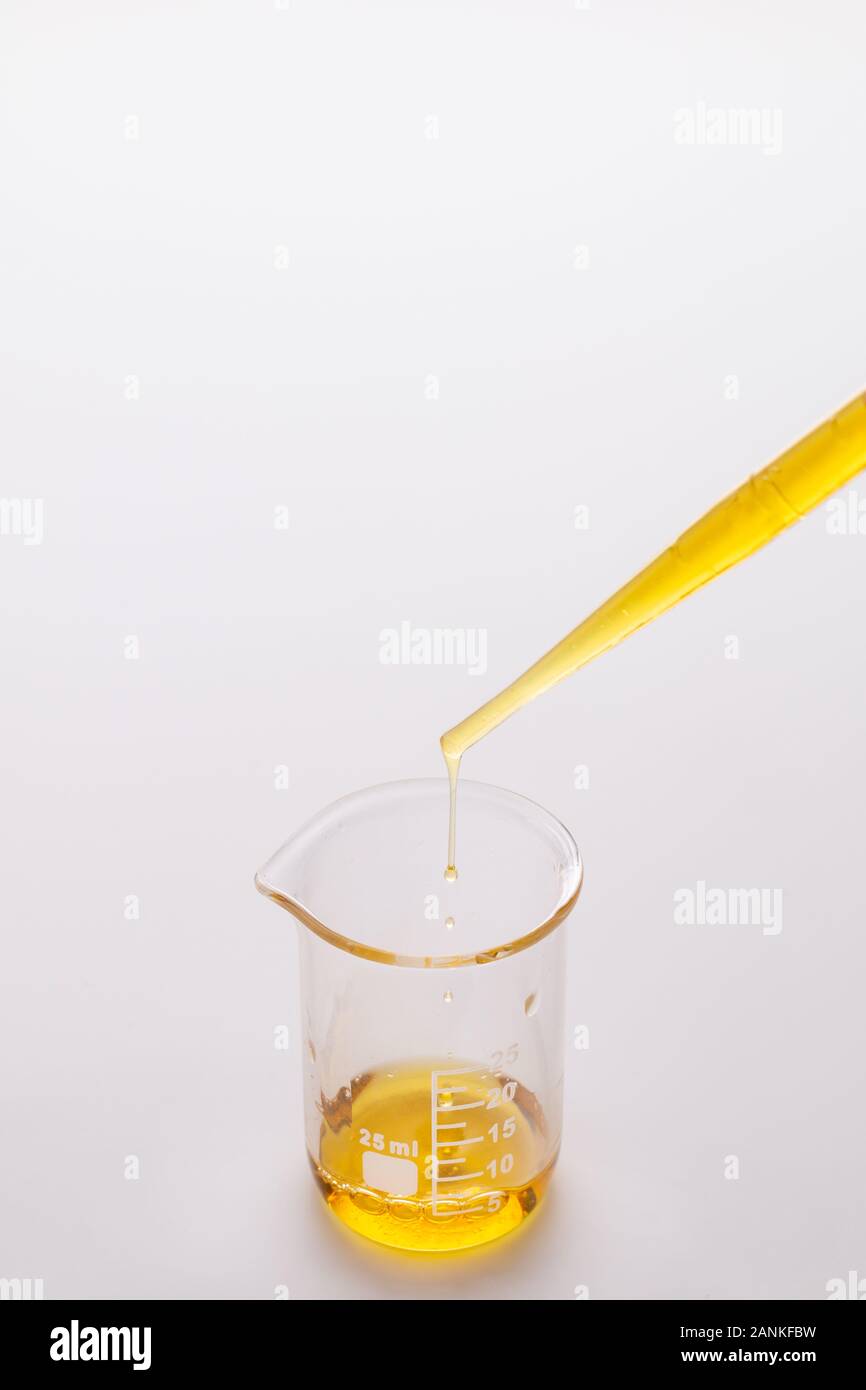 dropping sesame oil from a plastic pipette into a glass beaker, a ...