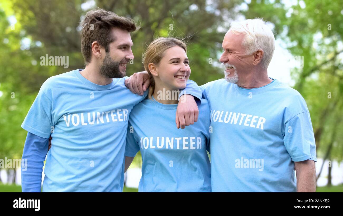 Three cheerful activists in volunteer t-shirts hugging, eco project ...
