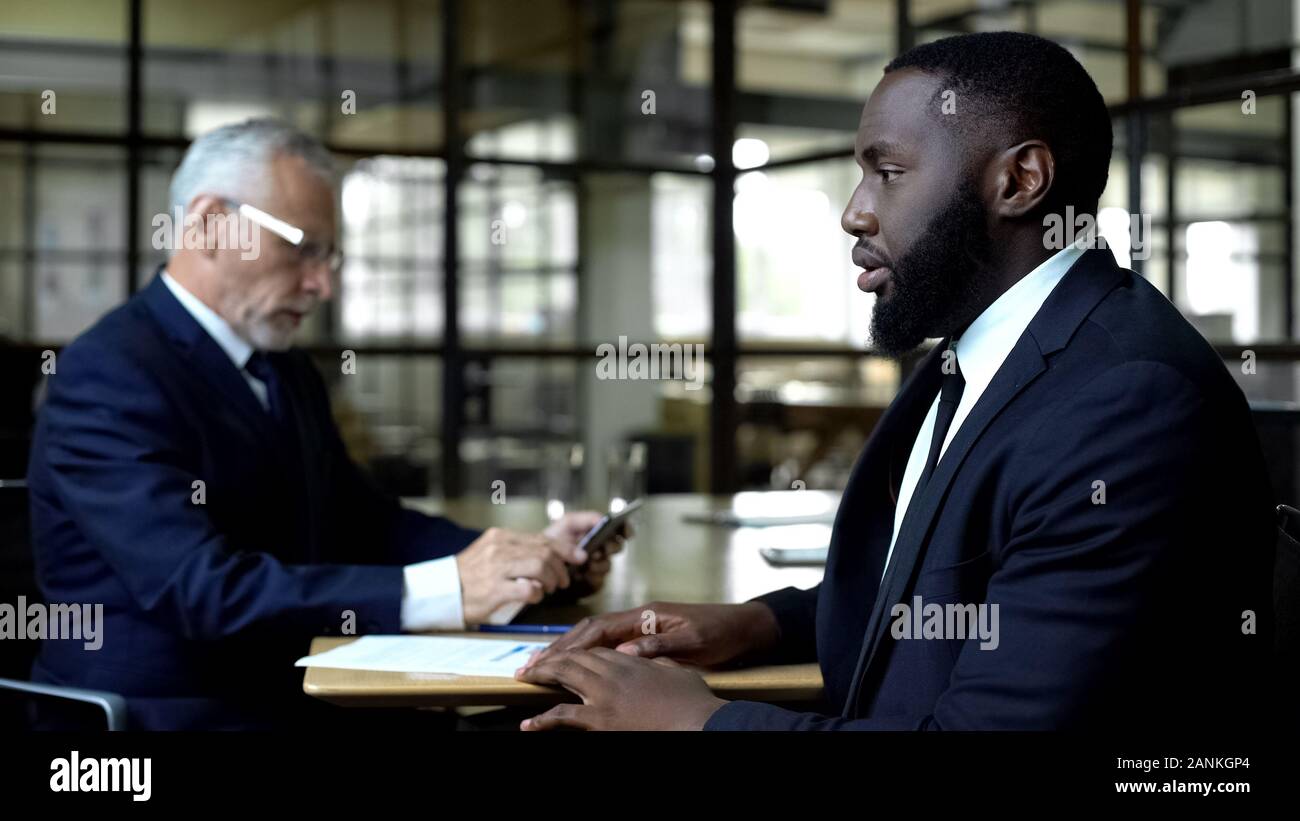 Nervous afro-american man at job interview, strict boss looking through ...