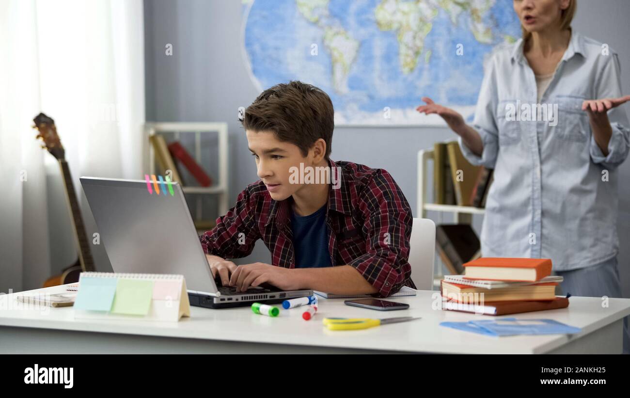 Angry mother shouting son playing laptop game instead doing homework ...