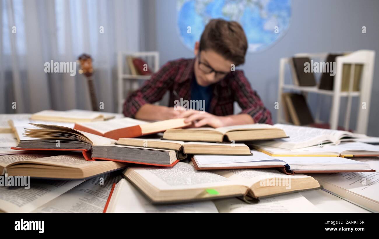 Table full of books, male student learning subject, smart student doing ...