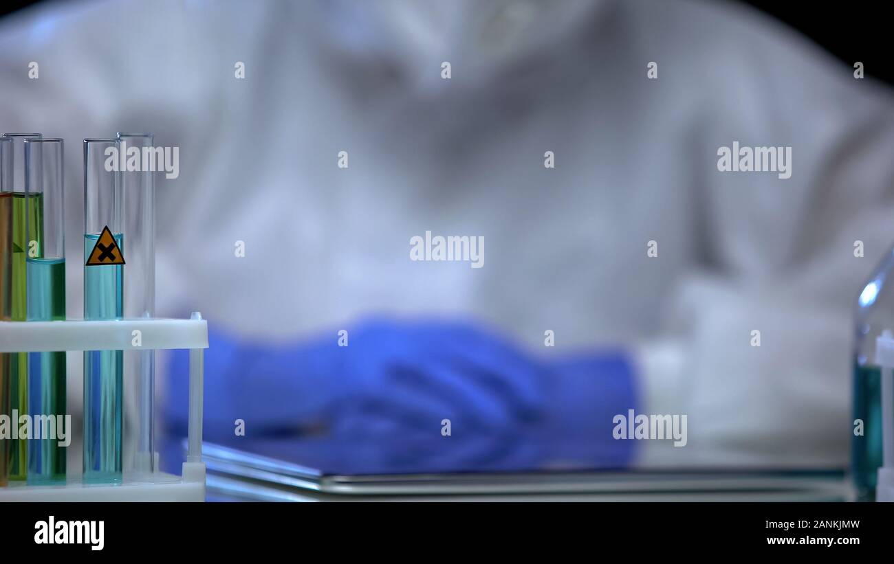 Toxic lab worker examining harmful liquid and reading notes on tablet ...