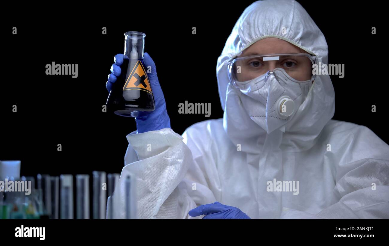 Woman in protective suit holding flask with dark harmful fluid, waste ...