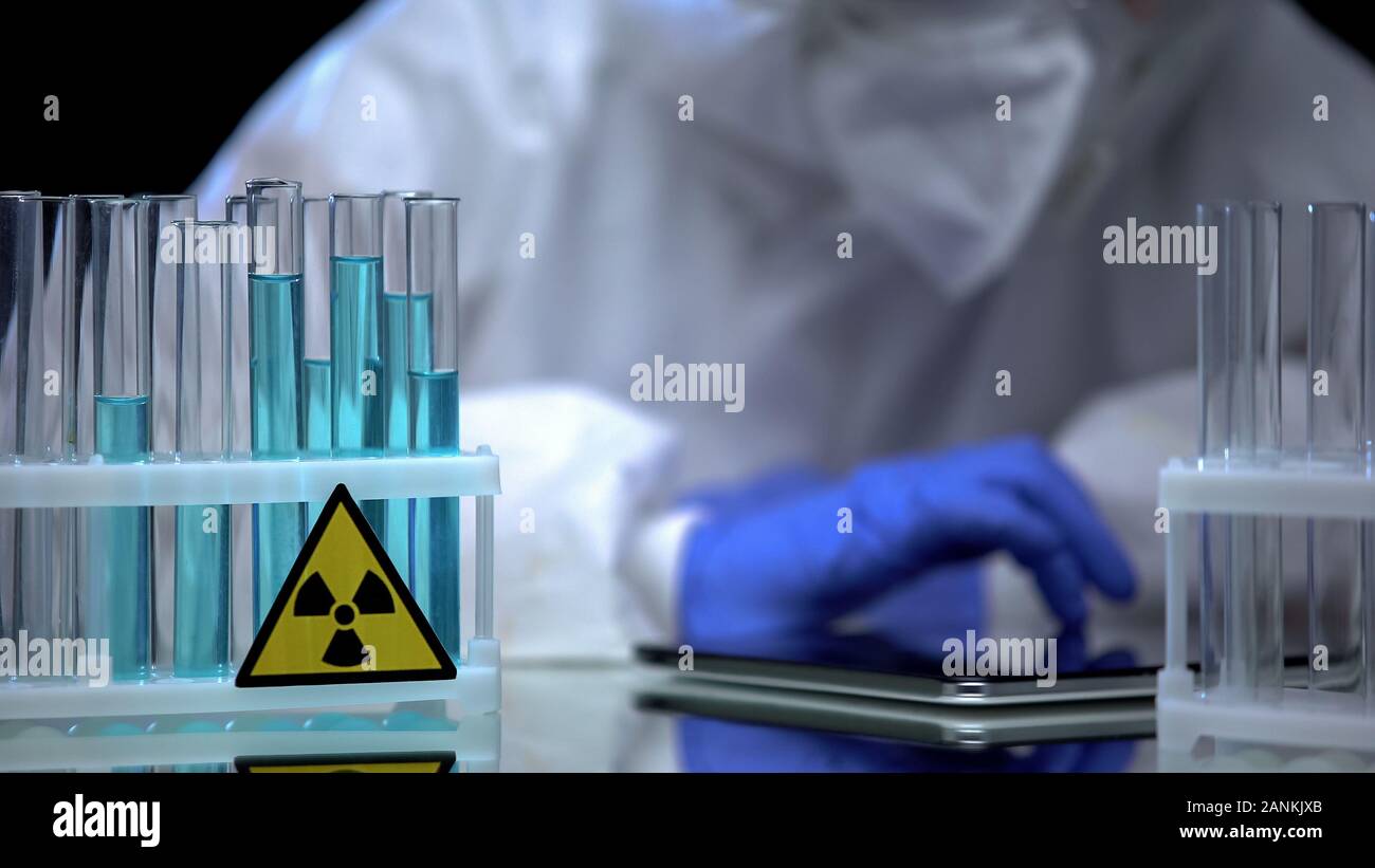 Lab worker in gloves testing blue radioactive liquid in test tube ...