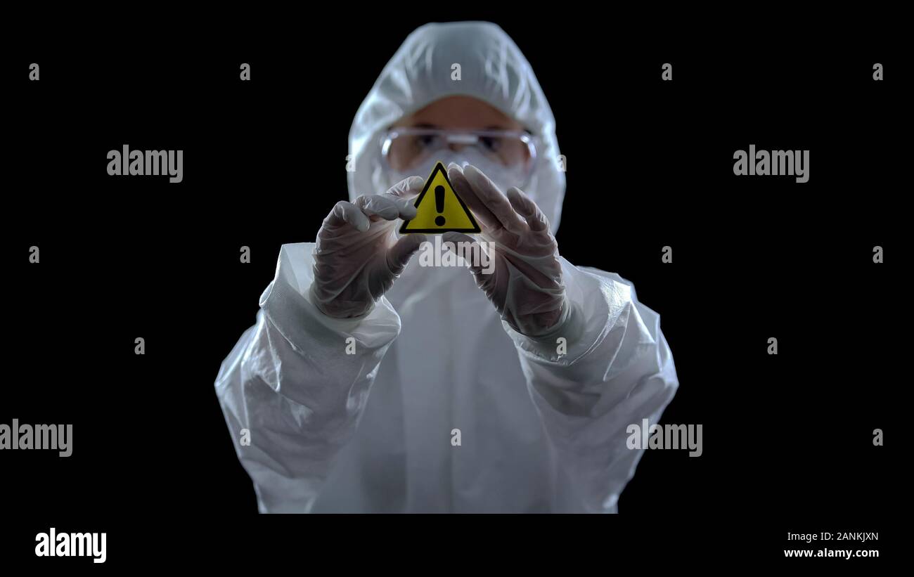 Lab worker in suit holding generic caution symbol in hands, black ...