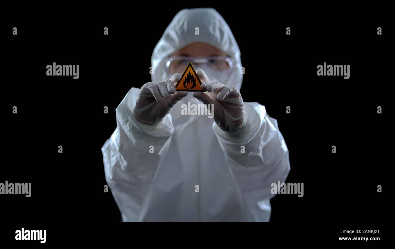 Lab worker in protective suit showing flame caution sign against dark ...