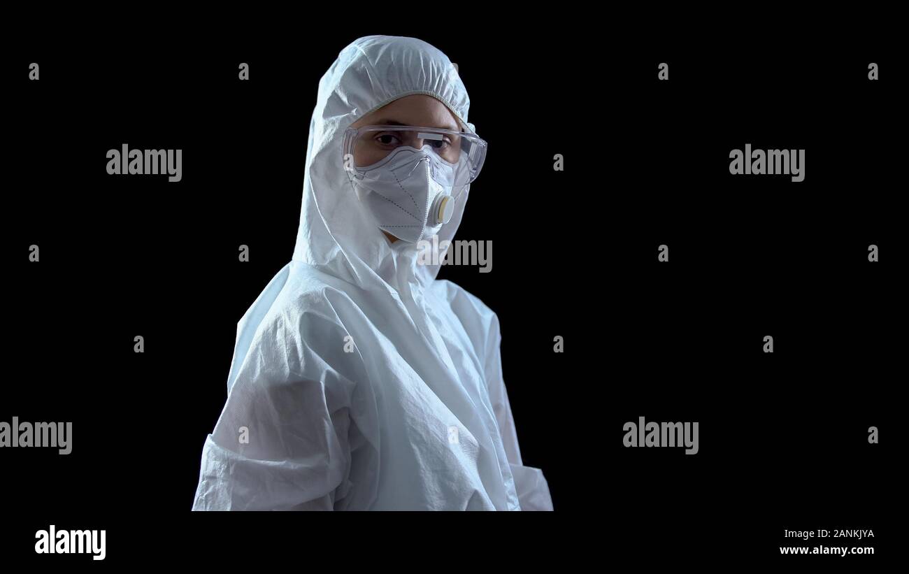 Lab worker in protective suit and mask looking at camera against dark ...