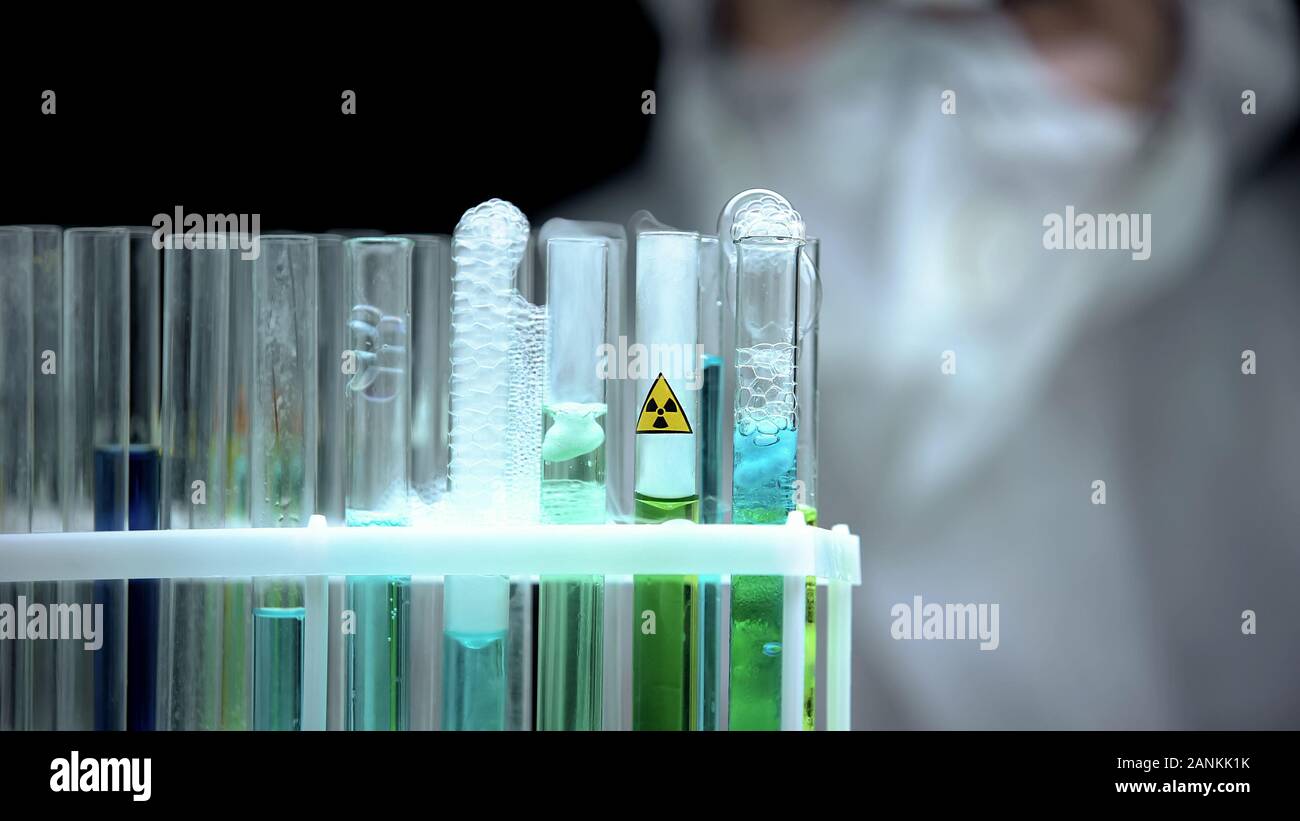 Lab scientist looking at test tubes with radioactive sample ecological ...