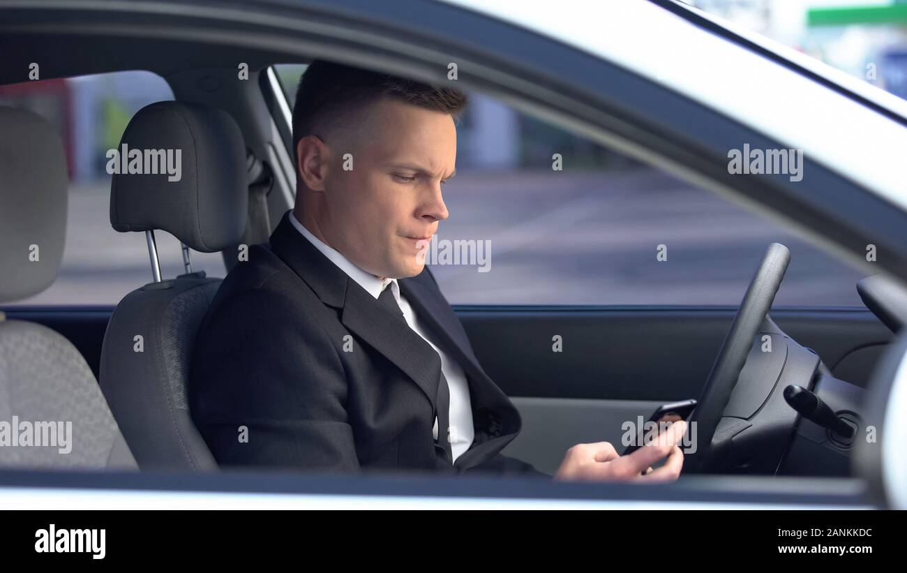 Nervous man in suit sitting on driver seat and calling on phone, late ...