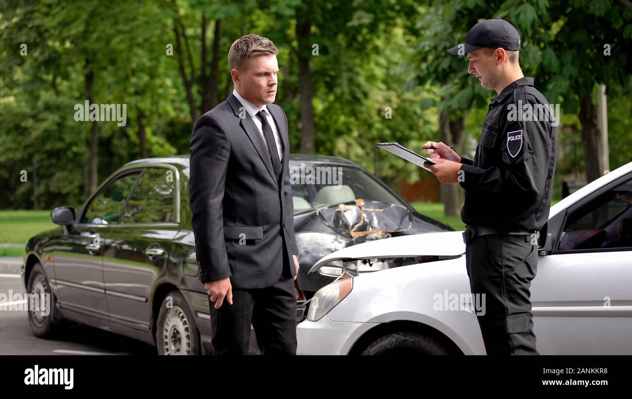 Male police officer filling car crash report, businessman standing ...