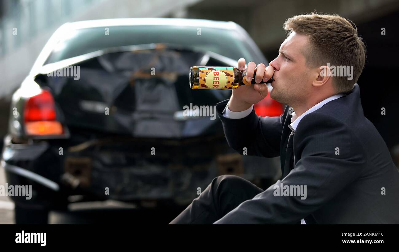 Irresponsible male driver drinking beer from bottle on crashed car ...