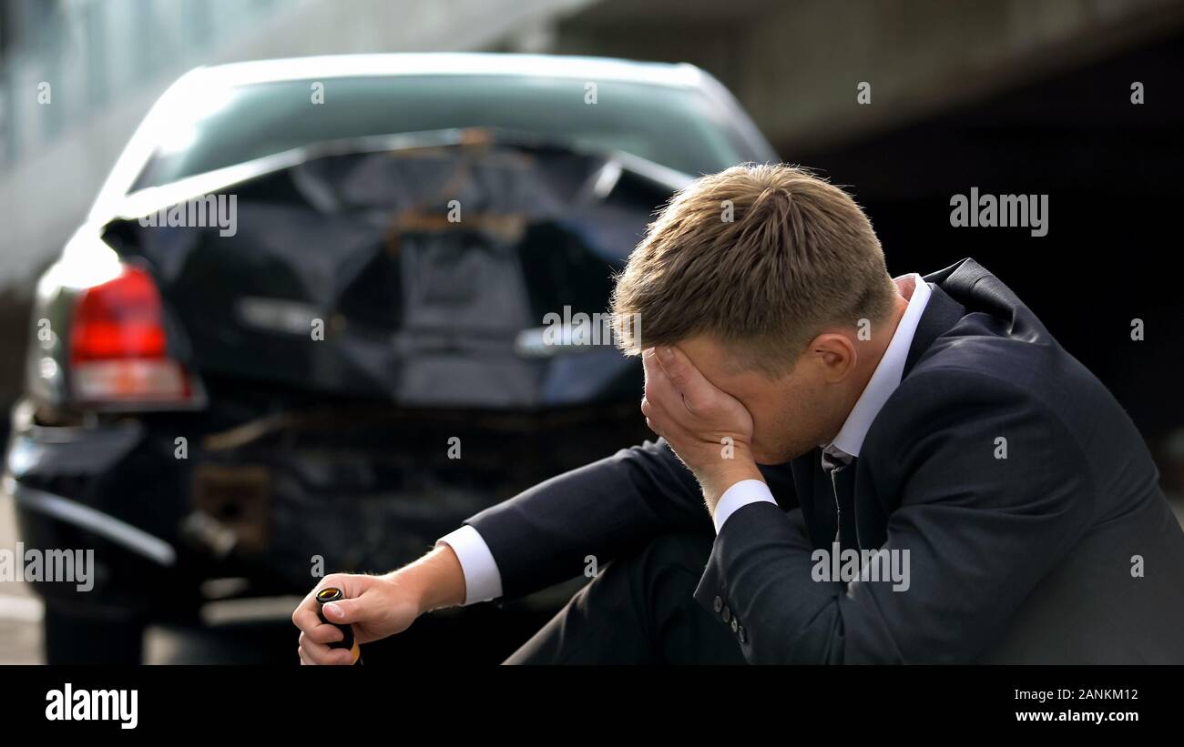 Drunk upset male driver holding bottle sitting street on crashed car ...
