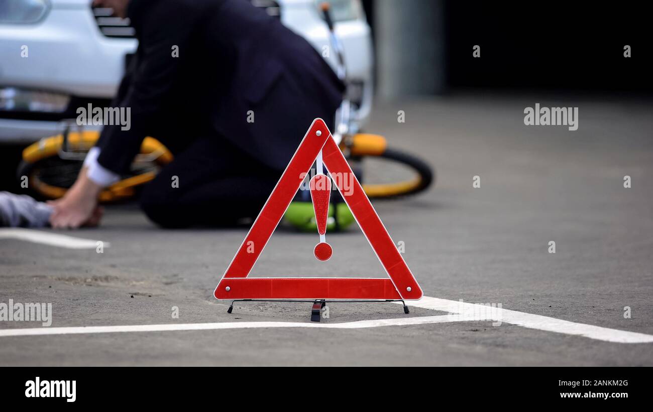 Emergency red sign on road, male driver checking car crash victim pulse ...