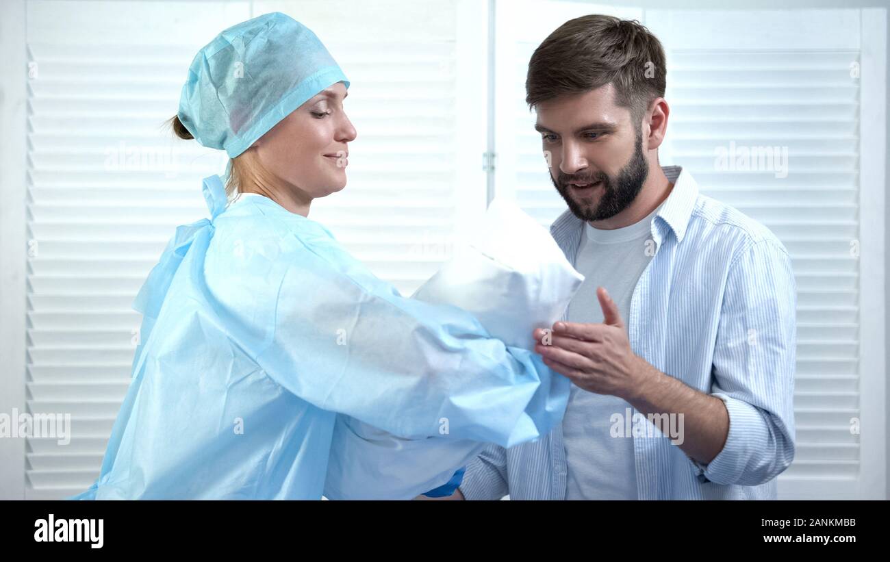 Smiling nurse giving young happy father newborn child, miracle of birth ...