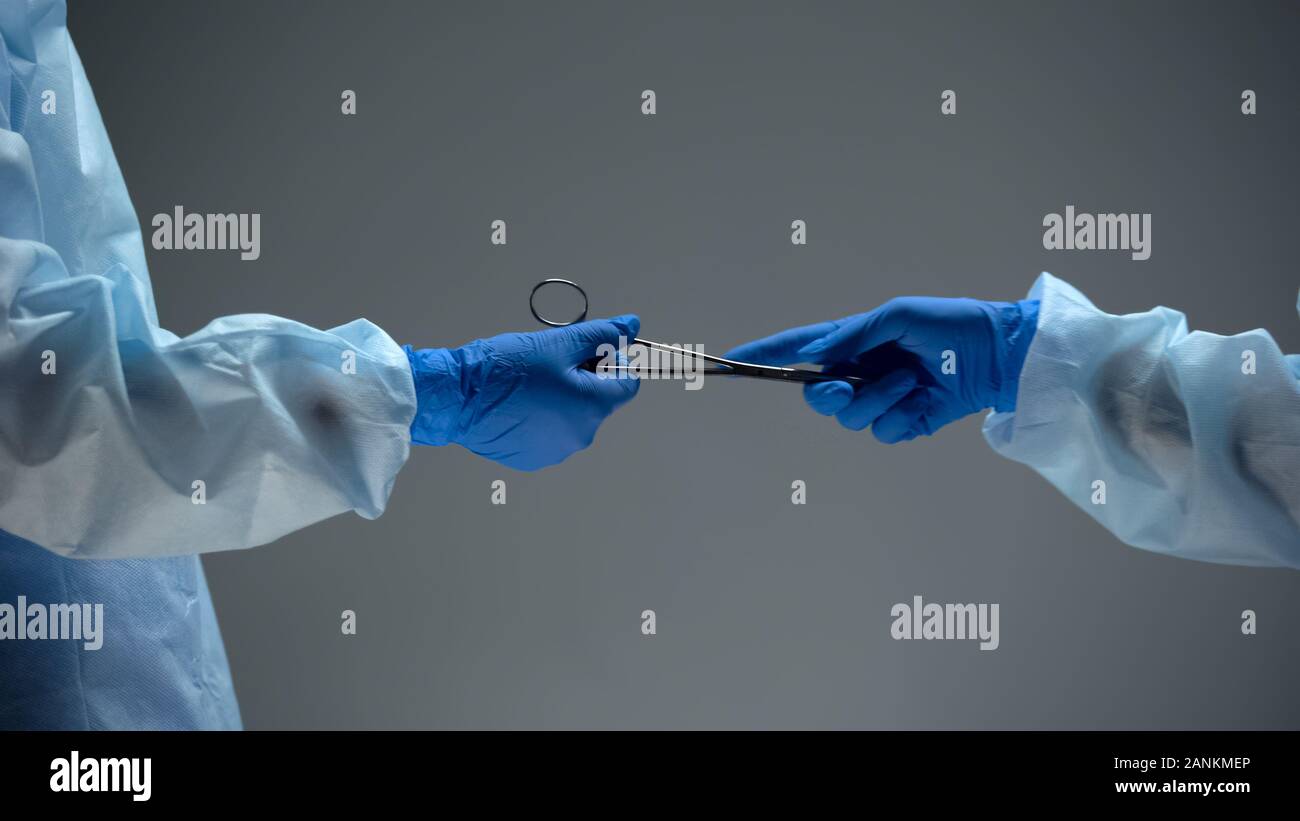 Surgeon giving scissors against dark background, illegal black-market ...