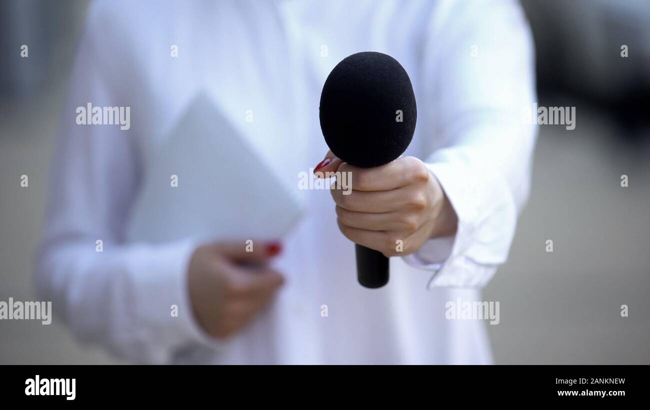 Female journalist with notebook proposing microphone, interviewing ...