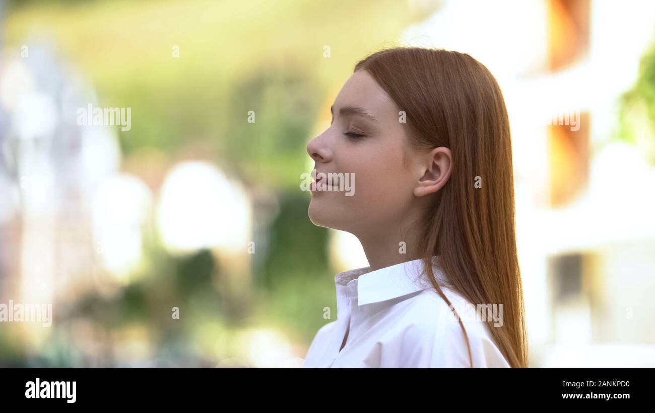 Inspired red-haired teenage girl inhaling pleasant aroma on city street ...