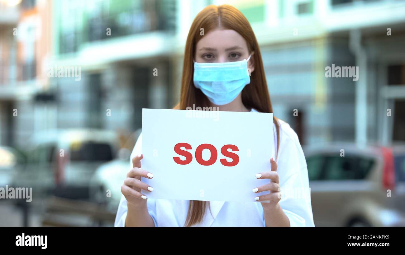 Young woman in protective mask holding sos sign, air pollution ...
